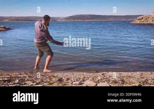 A young, attractive guy skipping stones on a mountain lake. High ...