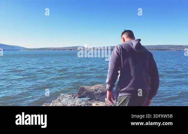 Young attractive tourist standing on the rocky shore of a mountain lake ...