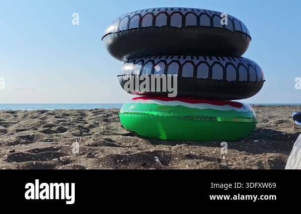Vibrant inflatable rings arranged neatly on a sandy shore under the sun ...