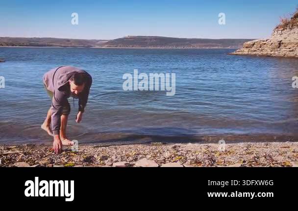 A young, attractive guy skipping stones on a mountain lake. High ...