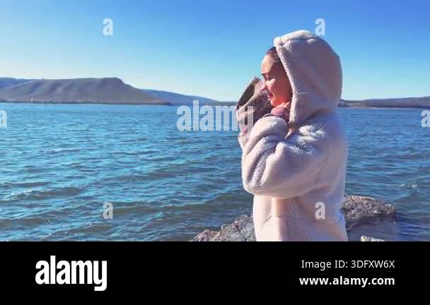 Young attractive girl traveler standing on the rocky shore of a ...