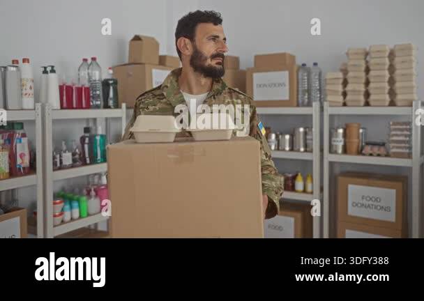 Hispanic man in military uniform holds box in indoor volunteer donation ...