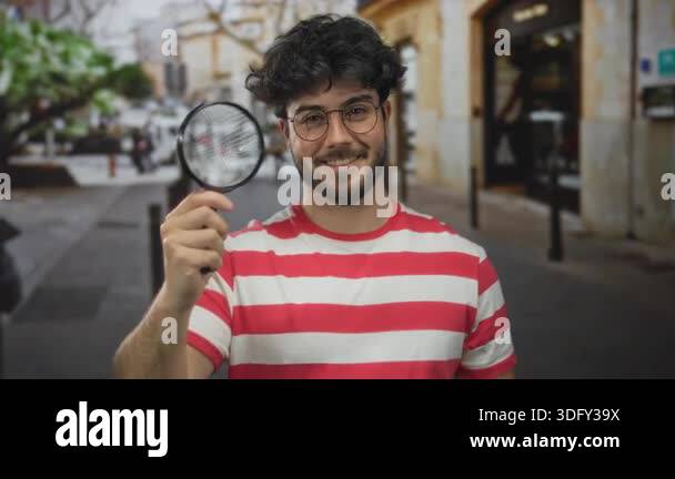 Young hispanic man with glasses and beard holding magnifying glass on a ...