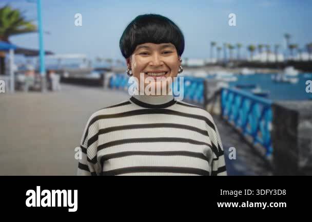 Young smiling woman standing by the seaside promenade with boats and ...