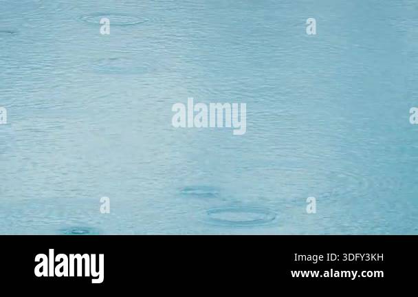 Raindrops falling on the smooth surface of the pool. Slow motion Mid ...