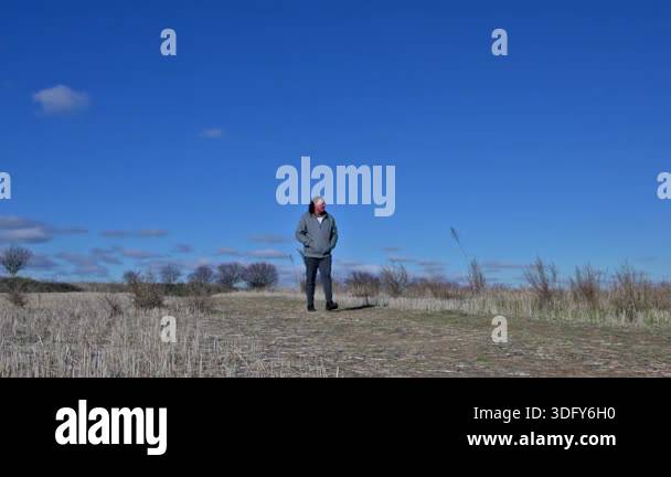 Adult man with long hair walking alone on a path in a barren ...