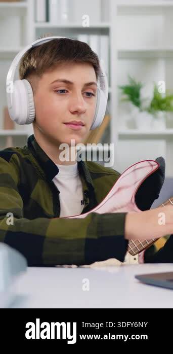 Attaractive boy in headphone is learning to play the guitar using ...