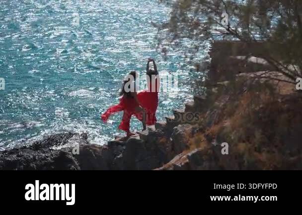 Girls in red dresses standing at ocean cliff beach Stock Video Footage ...