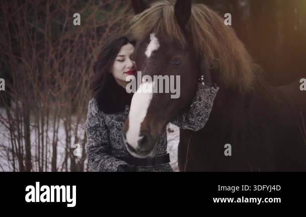A young brunette cowgirl taking care of mare riding horse while winter ...