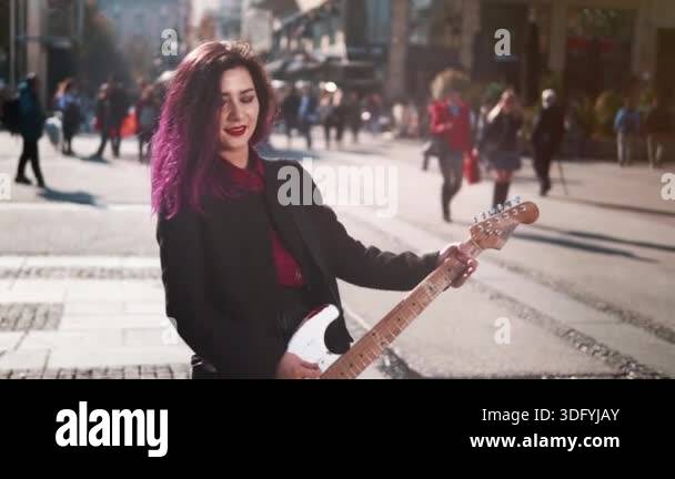 Daring rebel woman with purple hair playing electric guitar at city ...