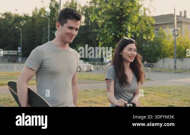 Two teenagers walking along city street with scooter and skateboard or ...