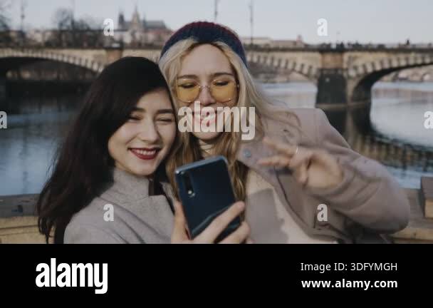 Portrait of two girlfriends in front of bridge and embankment of river ...