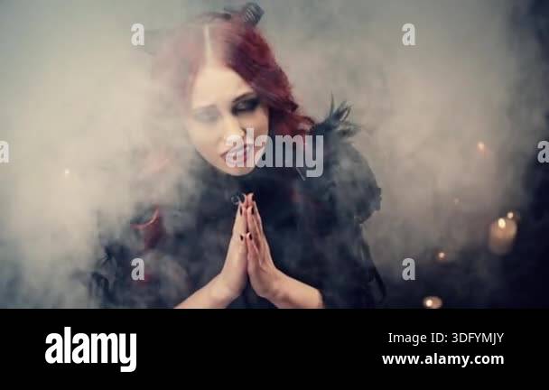 Red-haired girl witch with black horns sitting on floor in candlelight ...