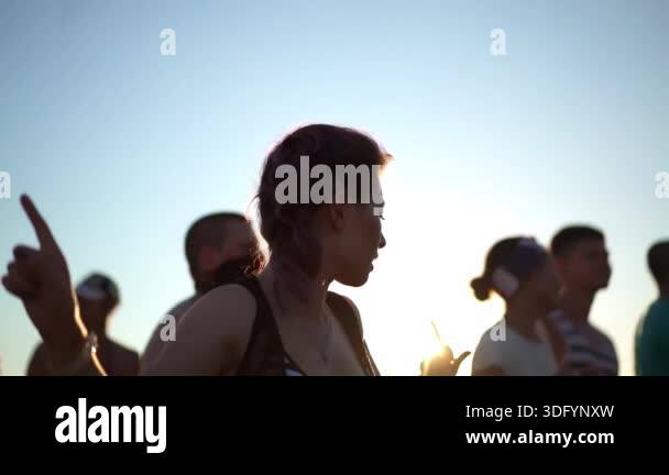Pretty asian woman dancing at sunset light among the crowd of people at ...