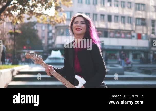 Daring rebel woman with purple hair playing electric guitar at city ...