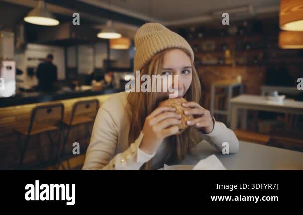 Young woman eating burger in fast food restaurant. American style ...
