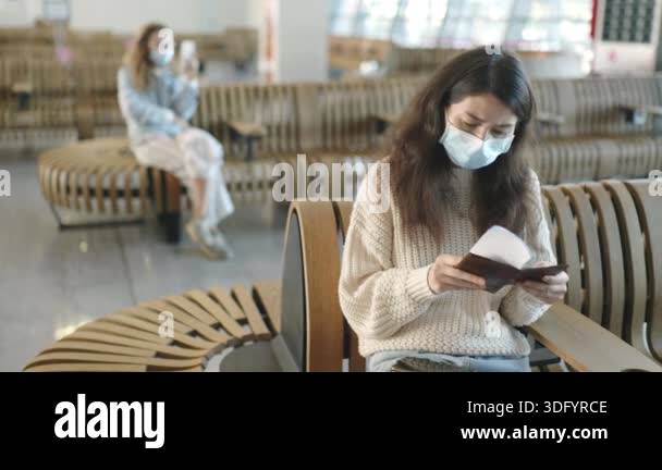 Young woman wearing medical mask sitting alone in airport terminal and ...