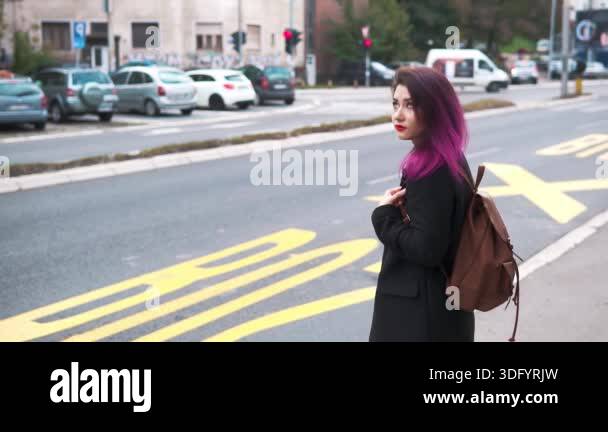 Pretty asian hipster girl waiting at a bus stop on a busy street. Pink ...