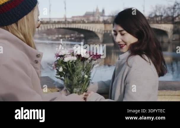 Close friends meeting on river embankment and exchanging bouquet of ...