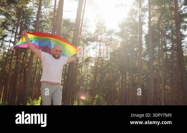 Happy queer man waving rainbow gay flag on sun flare light in beautiful ...