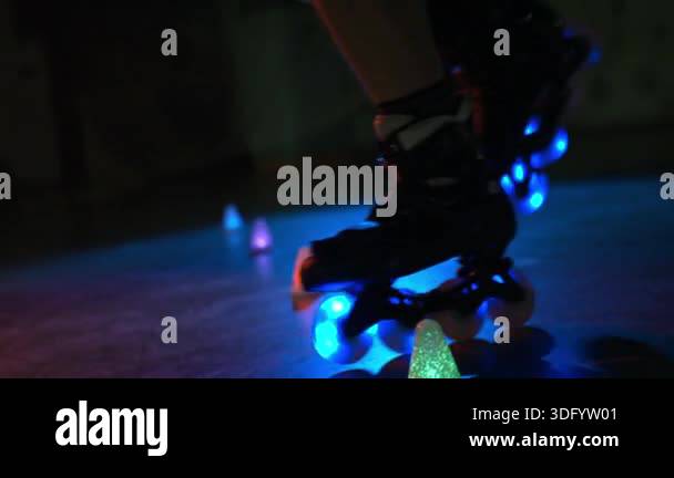 Close-up of teenager trick roller skating in dark studio with colourful ...