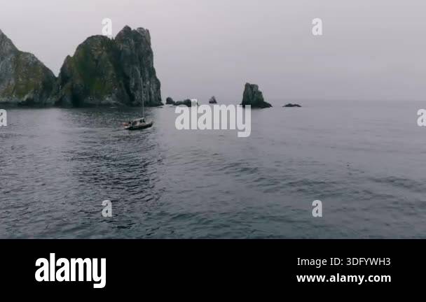 Small boat or ship sailing up to stone rocks in middle of sea or ocean ...