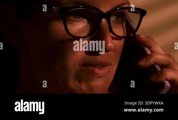 A close-up video of a woman wearing glasses, engaged in a phone ...
