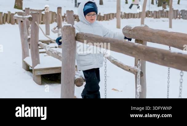 A child in winter clothing navigates a wooden obstacle course in a snow ...