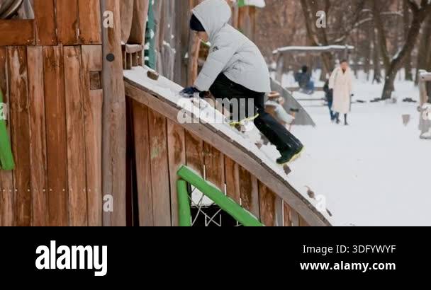 A child in winter clothing climbs and slides down a snowy playground ...