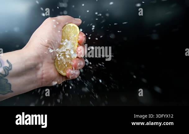 Male hand squeezing a half of lemon fruit. Juice bursting out on camera ...