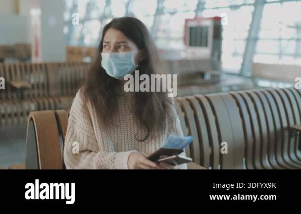 Young woman wearing medical mask sitting alone in airport terminal and ...