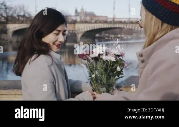 Close friends meeting on river embankment and exchanging bouquet of ...
