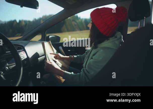 Pretty girl studying the map and sitting in car during her roadtrip ...