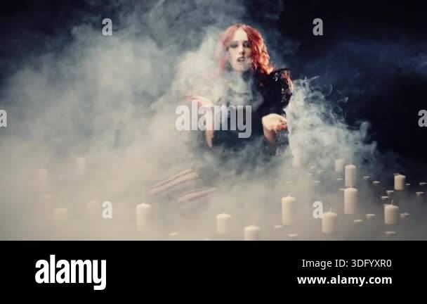 Young red-haired girl with devil horns and in black suit in dark room ...