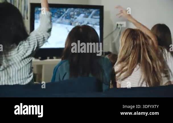 Backshot group of teens watching hockey match on tv celebrating goal ...
