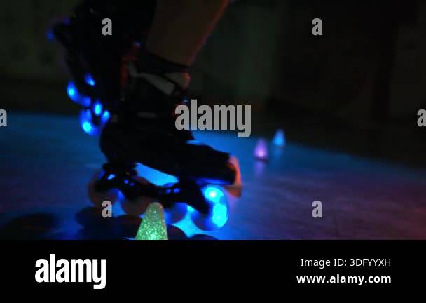 Close-up of teenager trick roller skating in dark studio with colourful ...