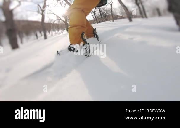 Closeup of snowboarder knee level sliding downhill through fresh powder ...