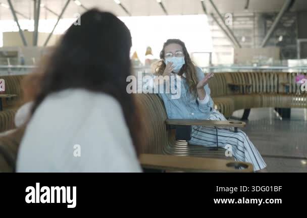 Two travelers women communicating in medical mask keeping safe distance ...