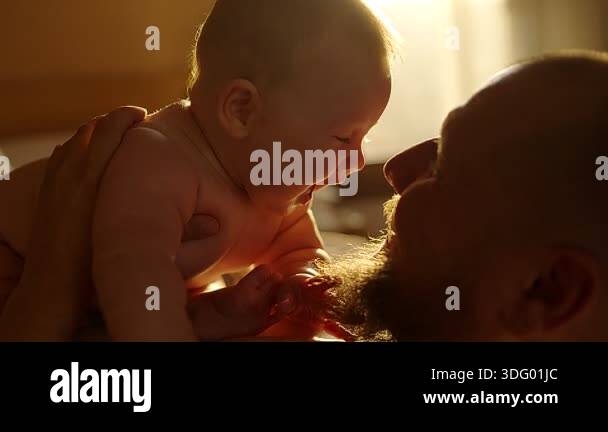 Young father with beard caressing and kissing his newborn baby kept by ...