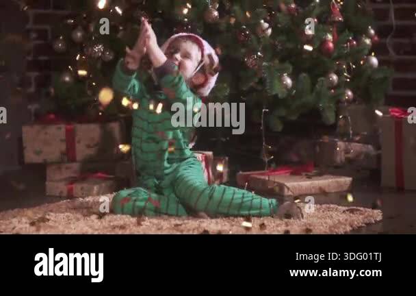 Happy little kid sitting under Christmas tree enjoying falling confetti ...