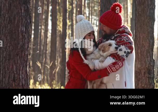 Happy young couple hugging in winter forest with their doggy. Xmas ...
