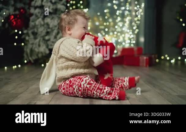 Joyful baby in rabbit sweater plays with red hat, drums feetand and ...