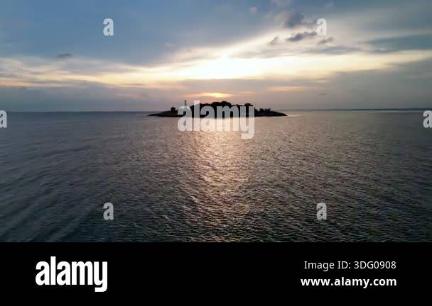 A small island is in the middle of the ocean. The water is calm and the ...