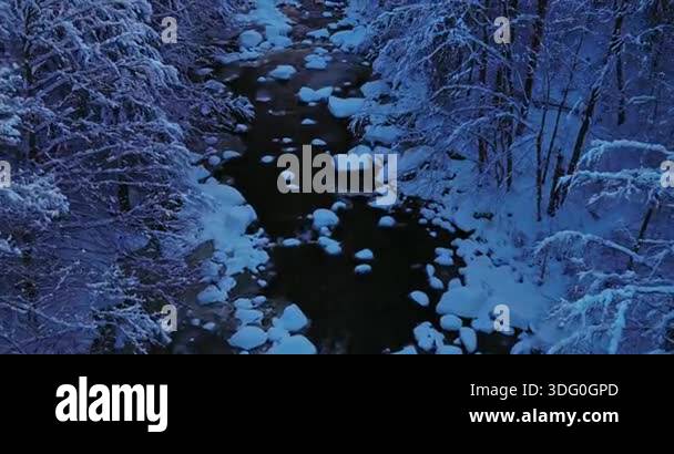 Peaceful flight over a snow-covered alpine stream. Flowing icy water ...