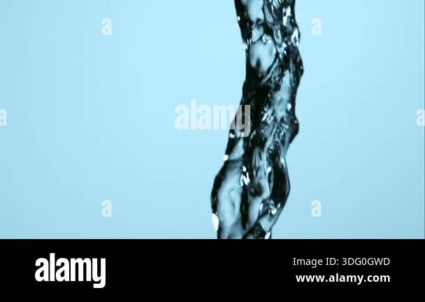 Thick twisted stream of clear water pouring down against light blue ...