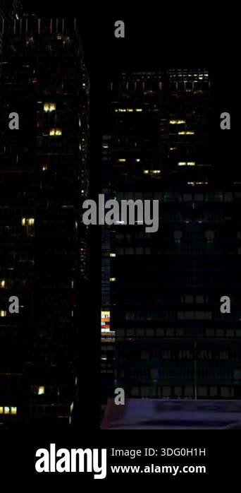 Upward tilt shot showing the illuminated windows of several tall, dark ...