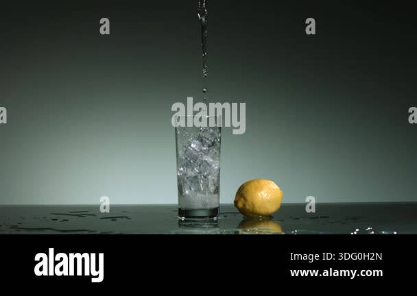 Clear fresh water pouring into tall glass filled with ice cubes ...