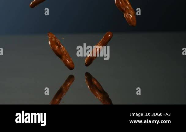 Several brown salted pretzels fall from above and bounce on a dark ...