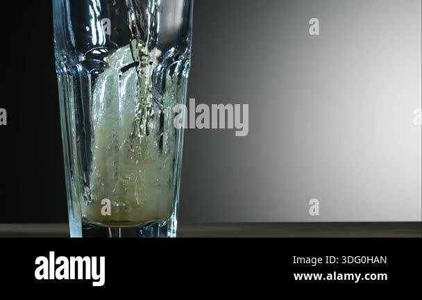 A bright yellow or golden liquid is poured from above into a faceted ...