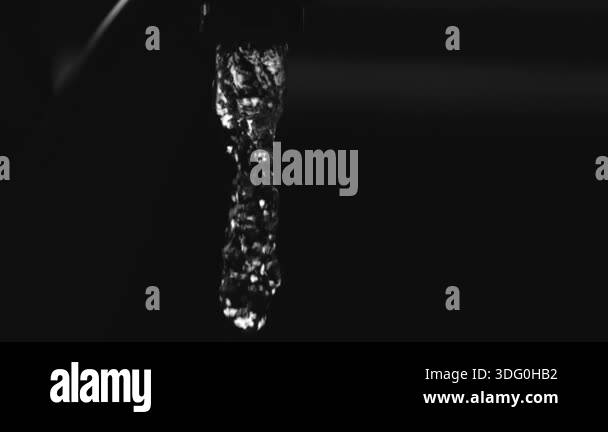 A steady stream of water pours from a metallic tap into a dark sink ...